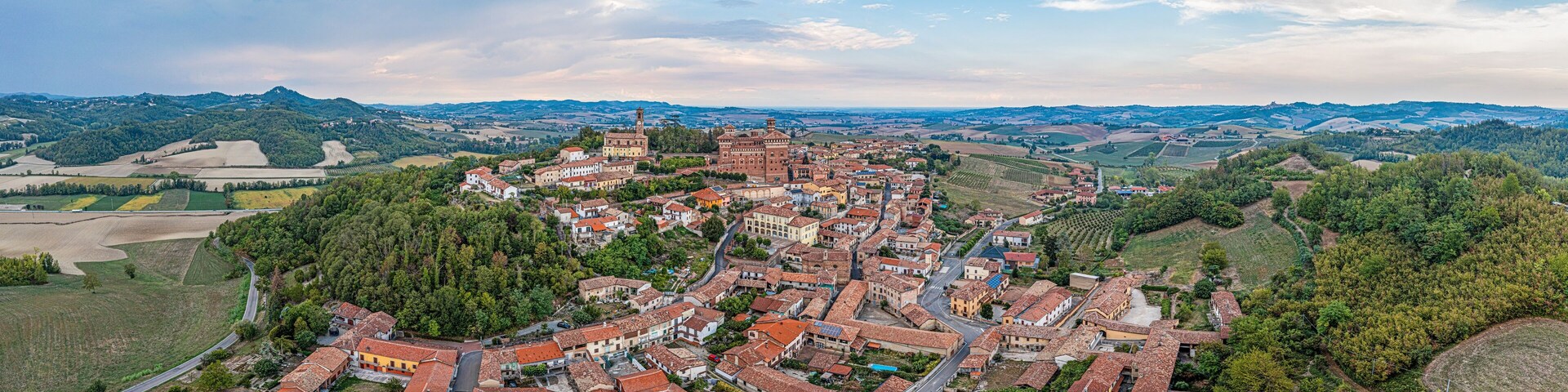 Vista aérea de uma cidade histórica com edifícios de telhados em terracota, cercada por colinas verdes exuberantes e vinhedos.