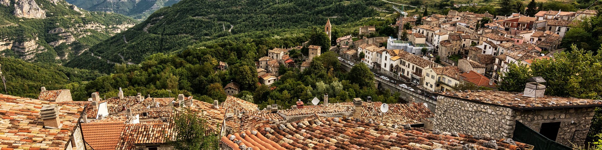 Uma cidade histórica com edifícios de telhados de terracota, um anfiteatro de pedra e colinas verdejantes ao fundo.
