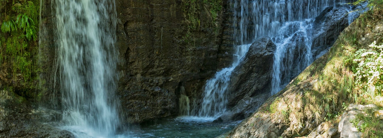 Uma cascata despencando sobre rochas em um riacho cristalino, cercada por vegetação exuberante.