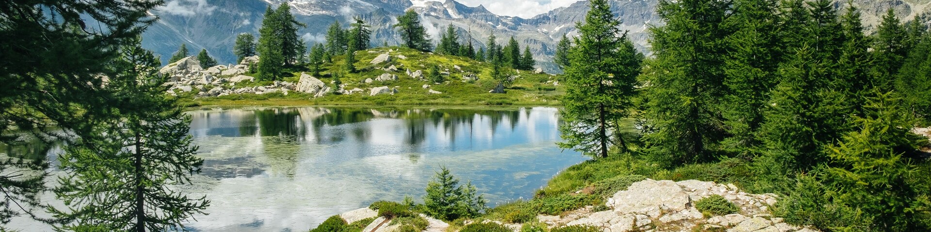 Um lago montanhoso rodeado por árvores perenes e terreno rochoso.