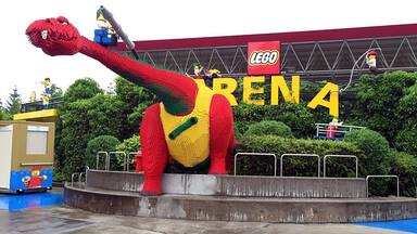 Uma estátua de dinossauro LEGO em frente a um edifício com o logotipo LEGO.