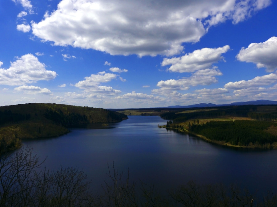 Um lago tranquilo rodeado por colinas arborizadas sob um céu parcialmente nublado.