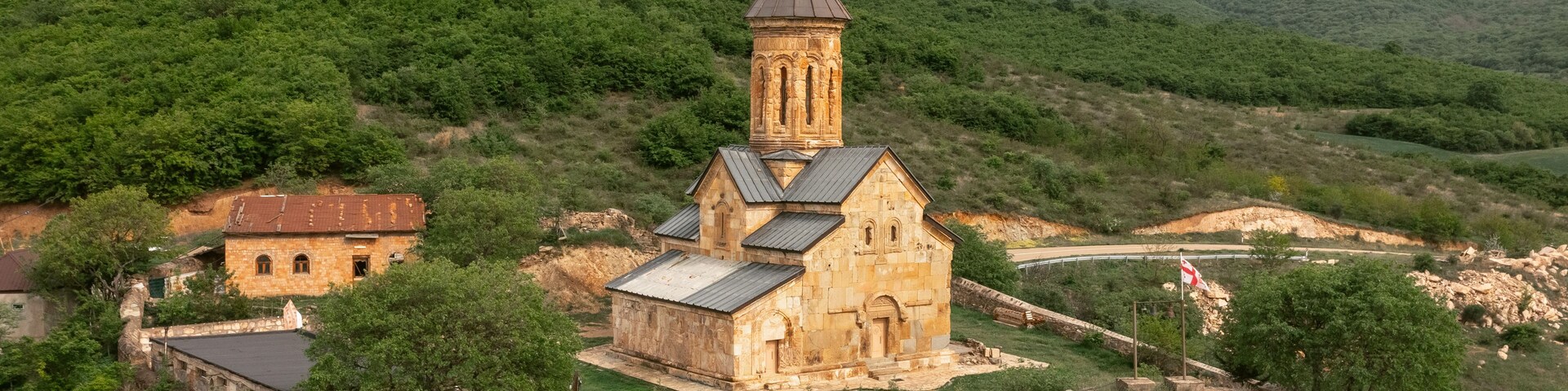 Uma igreja histórica com torre sineira, rodeada por colinas verdes e um arco de pedra.