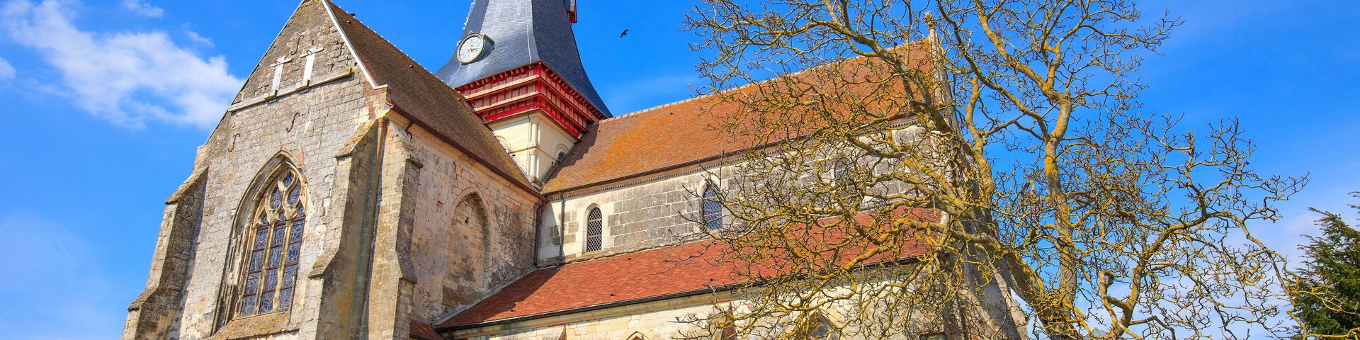 Uma igreja histórica com uma torre alta, janelas em arco e telhado de telhas vermelhas.