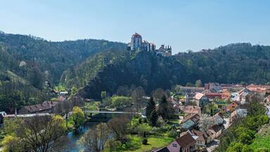 Um castelo numa colina com vista para uma cidade, um rio e vegetação.