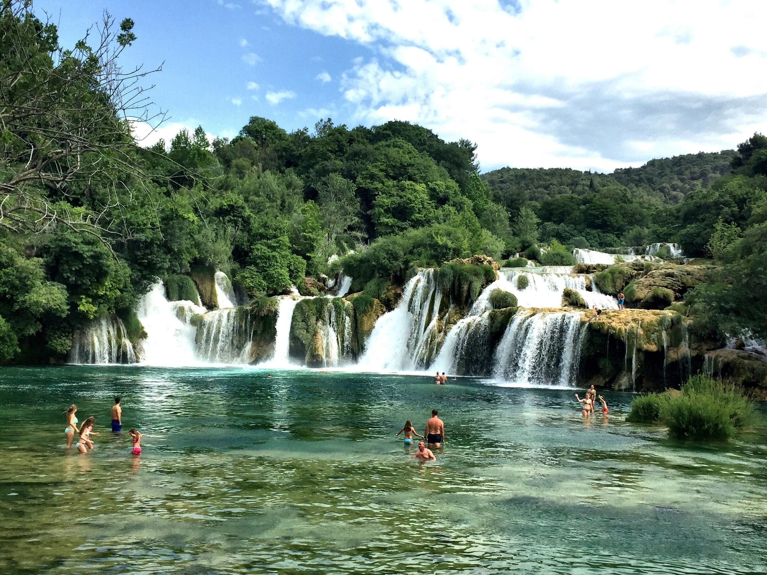 Uma cascata deságua em uma piscina límpida, cercada por vegetação exuberante.