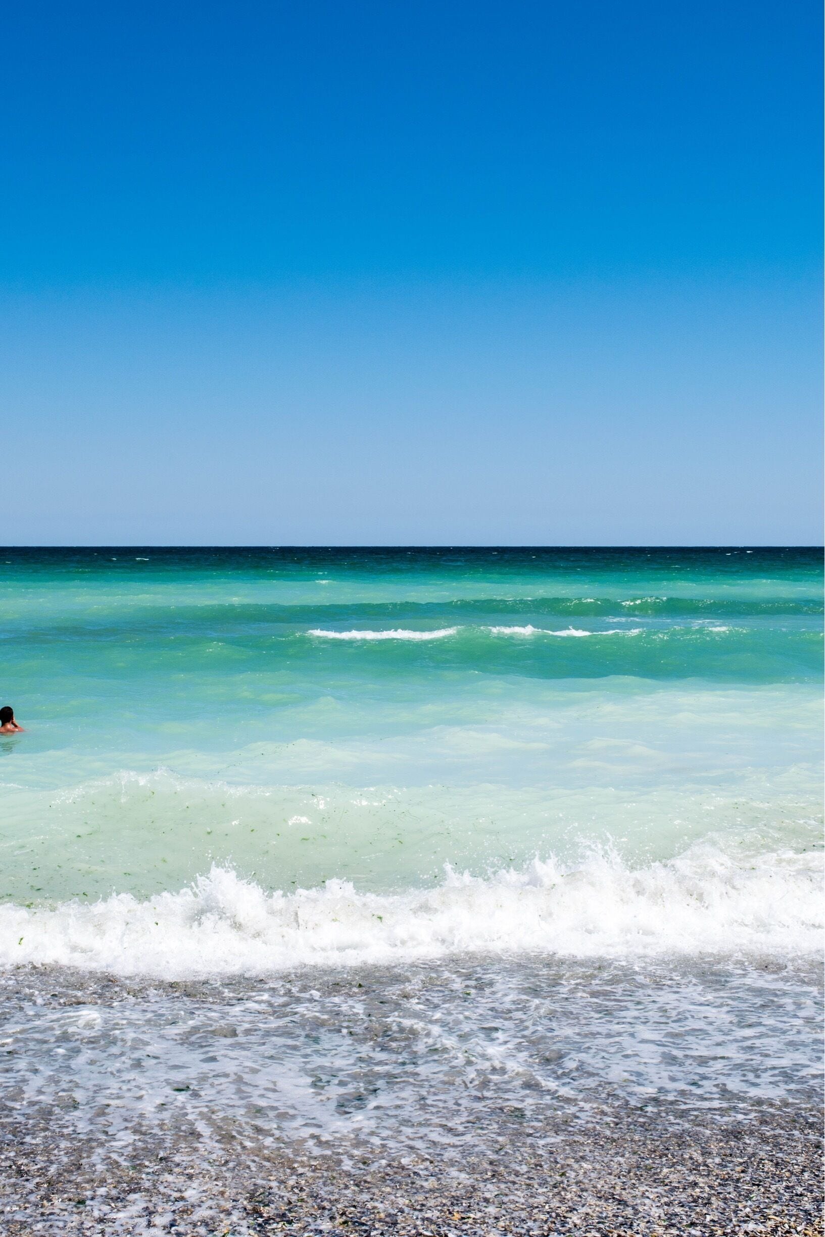 Uma praia com águas turquesa cristalinas e uma pessoa nadando ao longe.
