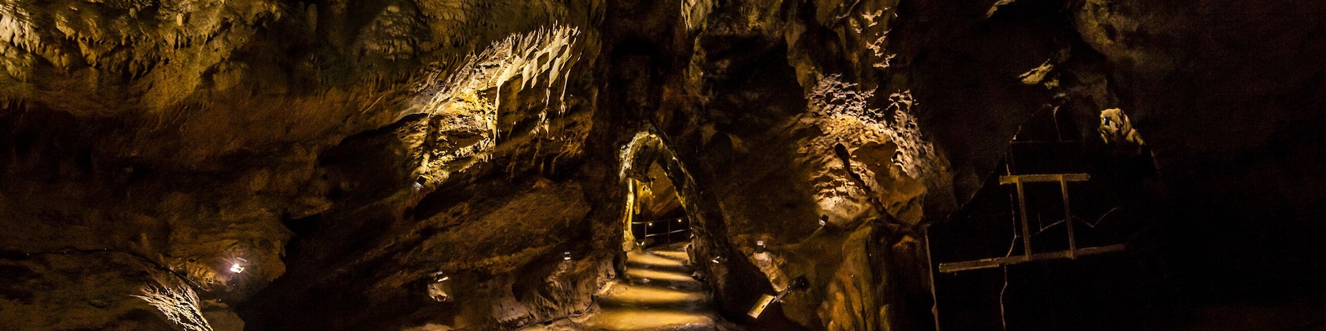 Uma gruta com estalactites, um tanque de água e uma escadaria que desce mais fundo.