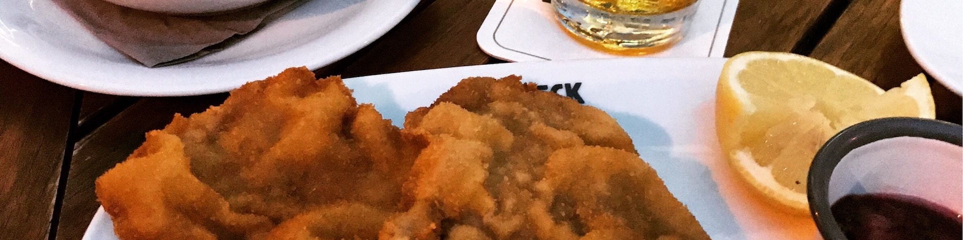 Um prato de peixe frito, um copo de cerveja, uma salada e uma fatia de limão sobre uma mesa de madeira.