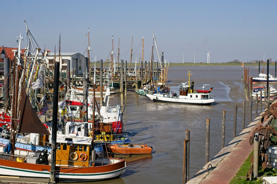 Uma marina com diversos barcos atracados, um rio e turbinas eólicas ao longe.