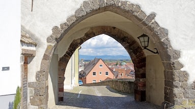 Um arco de pedra que dá acesso a uma rua de paralelepípedos, com edifícios tradicionais ao fundo.