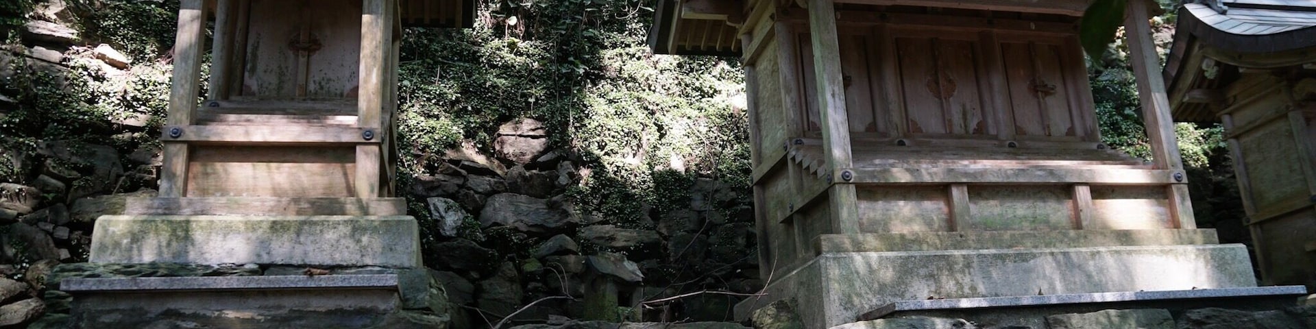 Duas construções de madeira tradicionais com bases de pedra, rodeadas por vegetação exuberante e terreno rochoso.