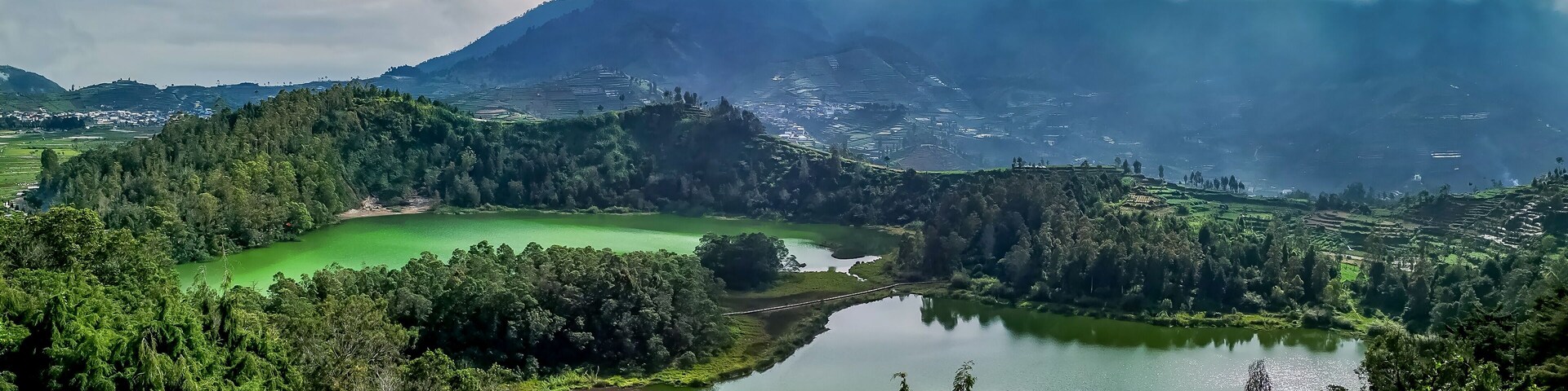 Paisagem montanhosa com um lago rodeado por floresta densa e campos em socalcos.