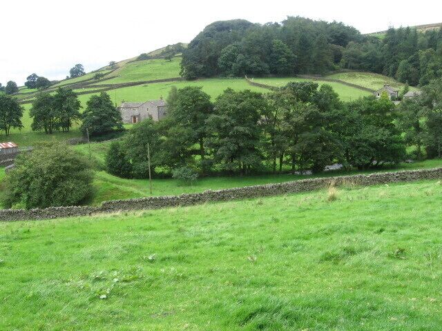 Paisagem rural com colinas ondulantes, um muro de pedra e uma casa ao longe.