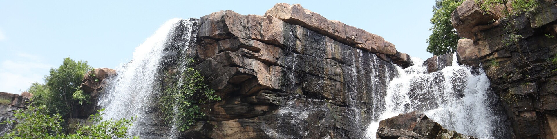 Uma cascata despencando por um penhasco rochoso, cercada por vegetação.