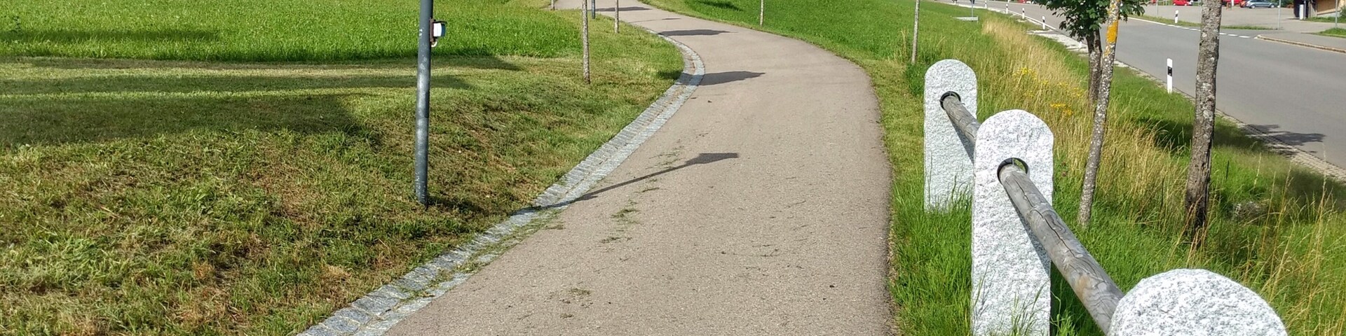 Um caminho pavimentado com uma cerca de pedra, uma igreja com uma cruz e um céu claro.