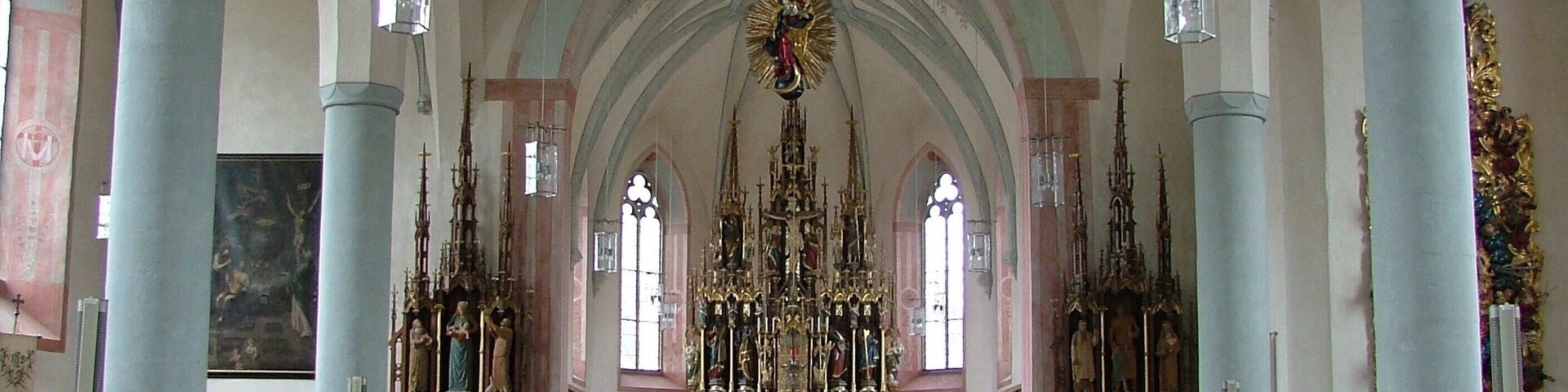 Interior de igreja com tetos abobadados, fileiras de bancos e um grande altar com estátuas religiosas.