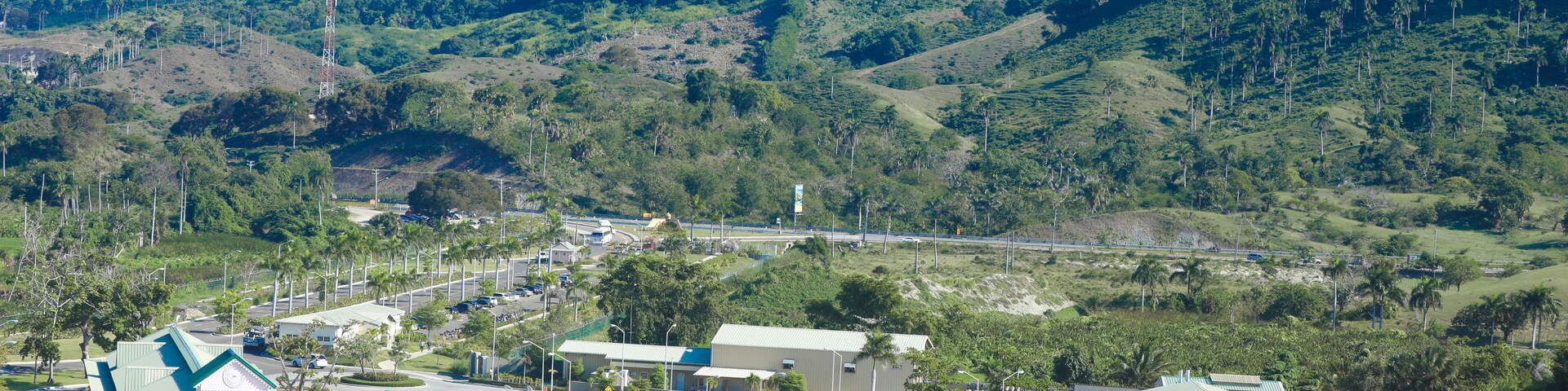 Uma cidade costeira com edifícios coloridos, uma estrada e colinas verdejantes ao fundo.