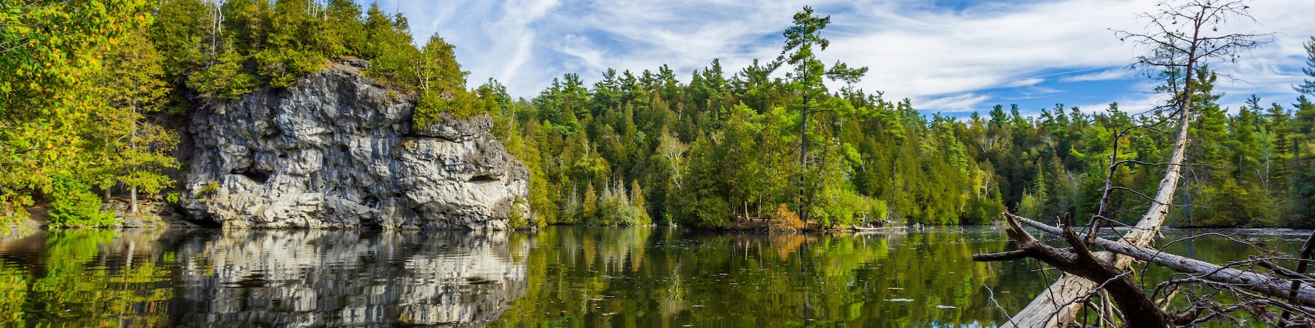 Um lago calmo com um penhasco rochoso e floresta densa.