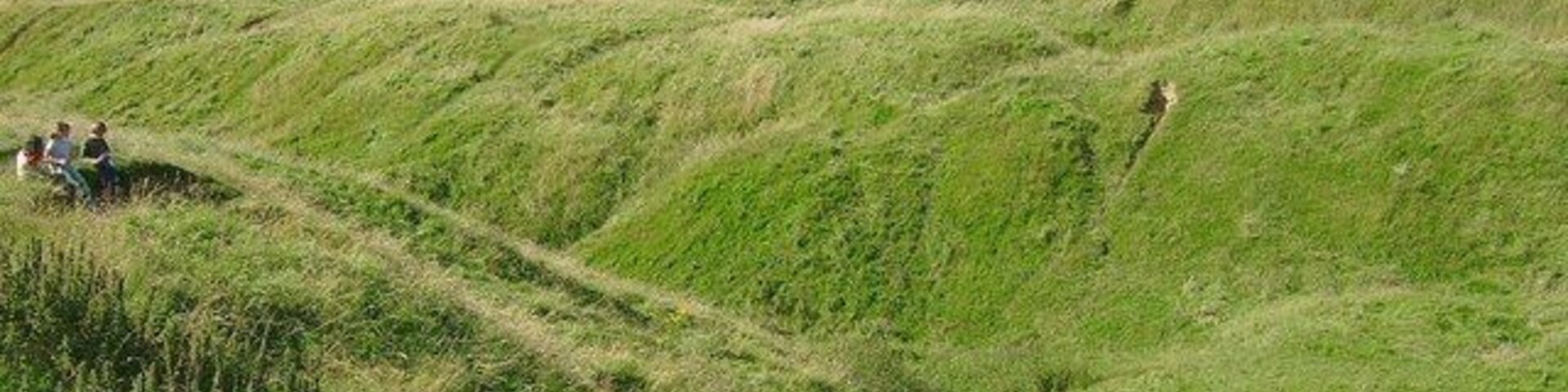 Colinas verdes e ondulantes, céu claro e um edifício ao longe.