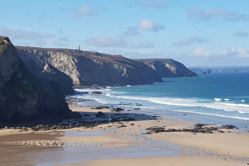 Paisagem costeira com falésias, uma praia de areia e o oceano.