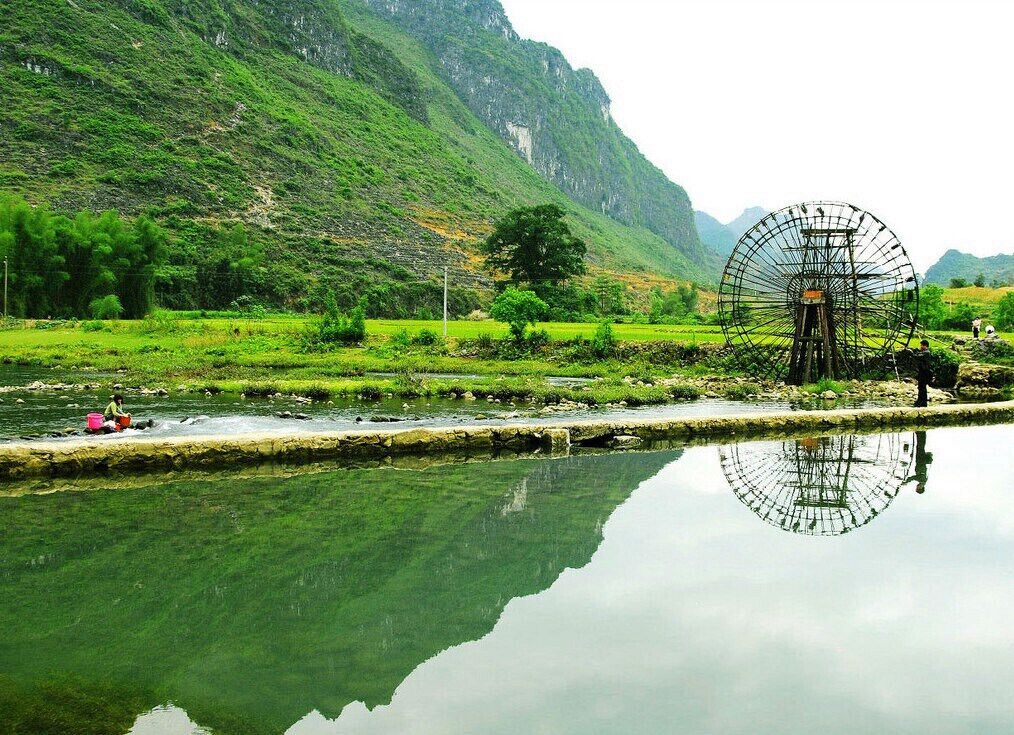 Um rio com uma roda d'água, colinas verdes exuberantes e um reflexo límpido na água.
