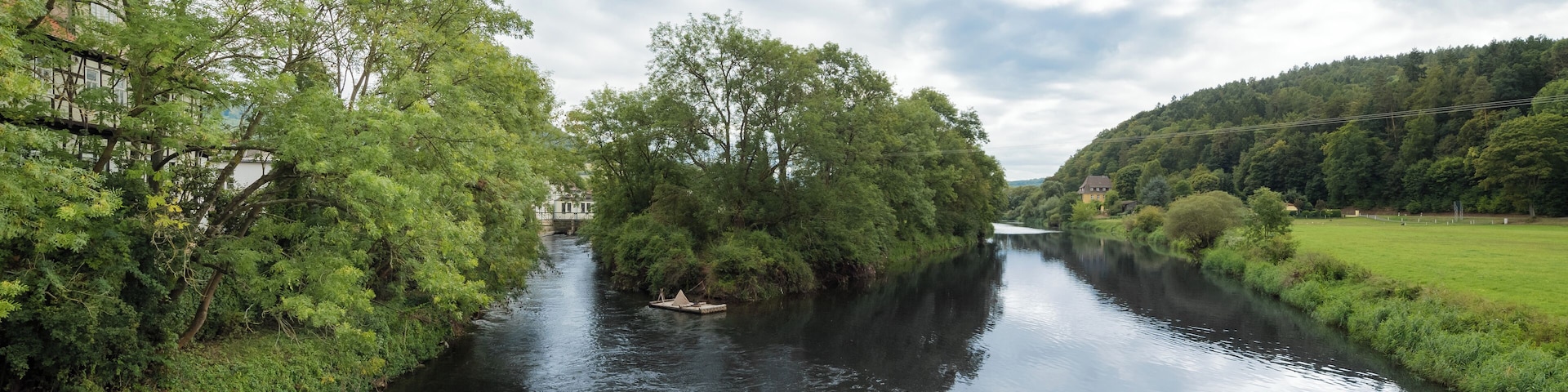 Die Werra bei Wanfried von der Wanfrieder Werrabrücke aus gesehen. Der linke Flussarm (Mühlgraben) dient zur Versorgung des Elektrizitätswerks Wanfried, dessen Gebäude im Hintergrund sichtbar ist. Vor der Insel in der Flussmitte ist ein Floß angelegt. Im linken Bildteil ist ein Teil der großen Schlagdhäuser zu sehen. Blickrichtung Süden.