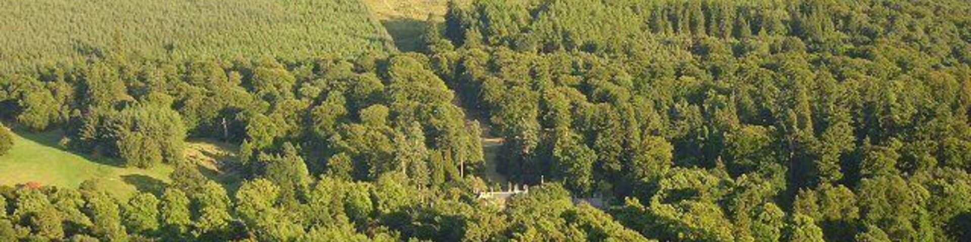 Paisagem montanhosa com florestas densas e um pequeno edifício ao longe.