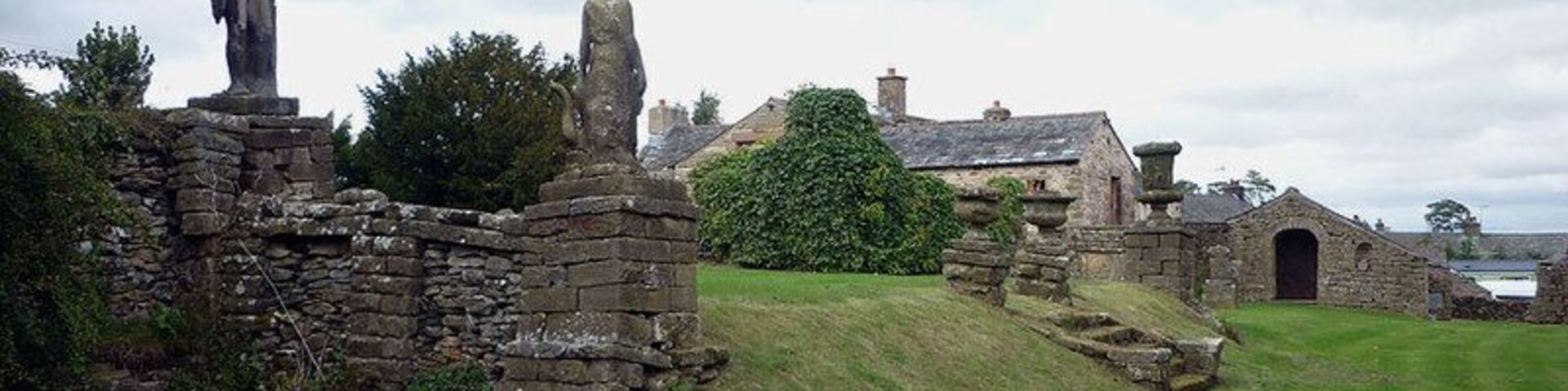 Uma construção de pedra com estátuas, um campo gramado e um edifício ao fundo.