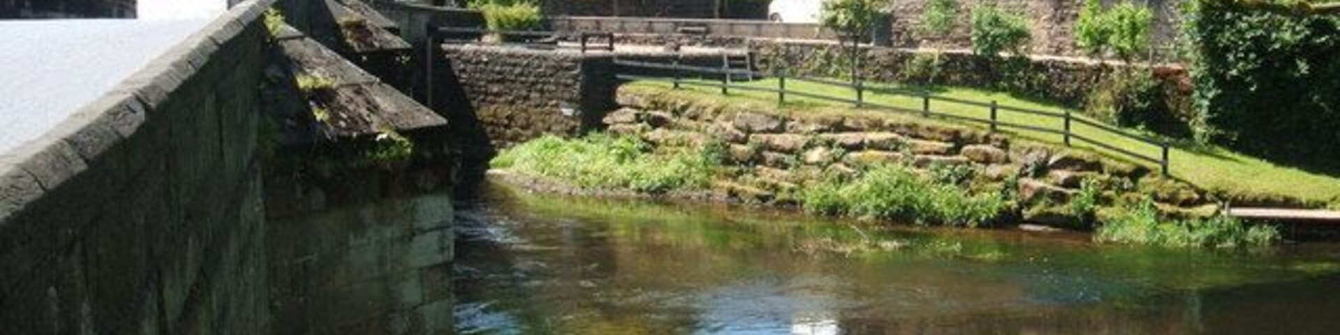 Uma ponte de pedra sobre um rio, rodeada por vegetação e edifícios históricos.