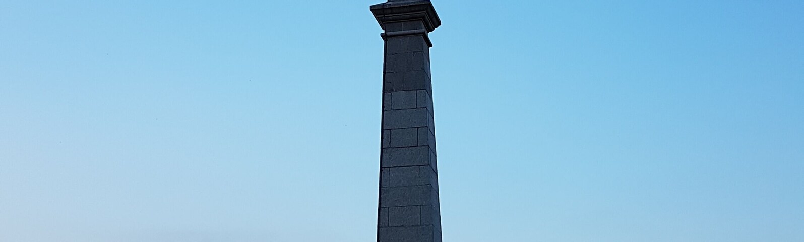 Um monumento alto com topo esférico e base decorada com quatro esferas.