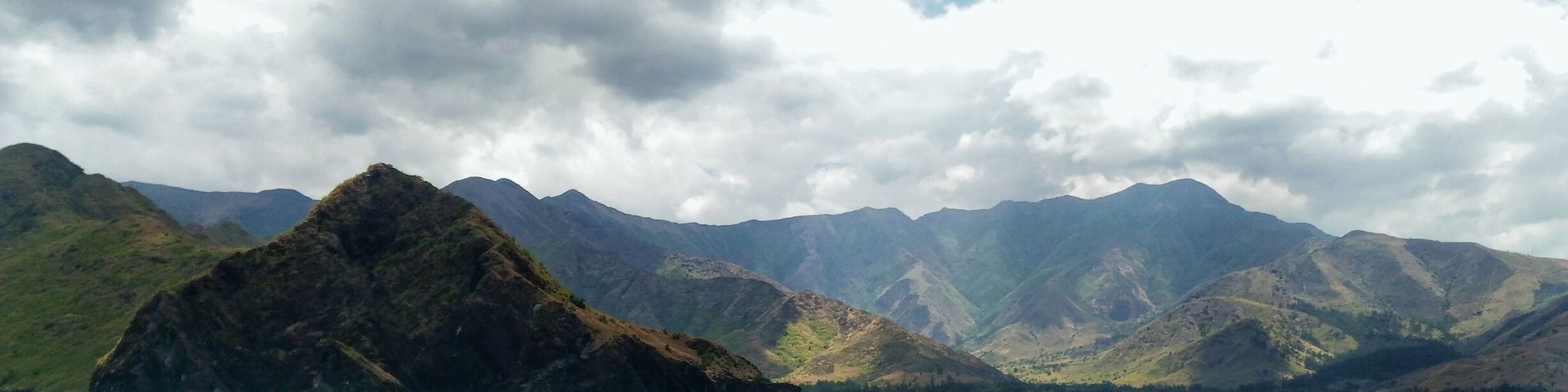Paisagem montanhosa com um pico rochoso em destaque no primeiro plano e um corpo d'água ao fundo.
