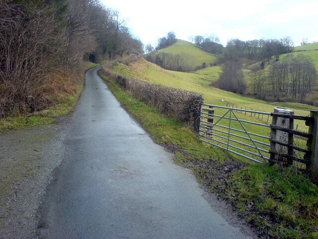 Uma estrada rural estreita ladeada por sebes e um portão de metal.