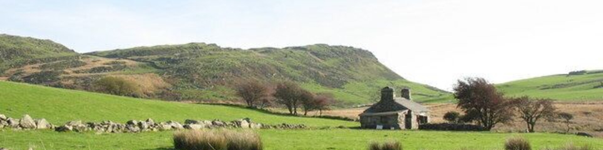 Paisagem rural com muro de pedra, construção de pedra, colinas ondulantes e ovelhas pastando.