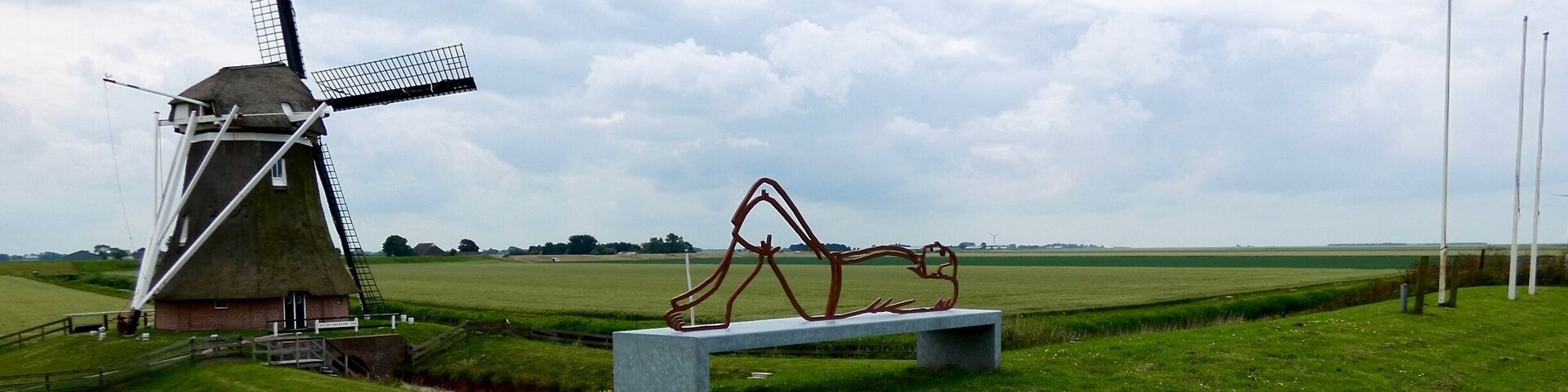 Um moinho de vento, um banco e uma escultura em um campo gramado.