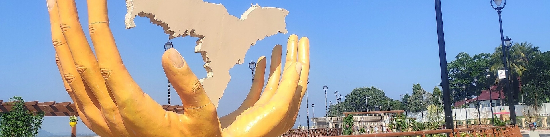 Uma grande escultura de mão dourada com o contorno de um mapa, cercada por uma grade de metal e postes de luz.