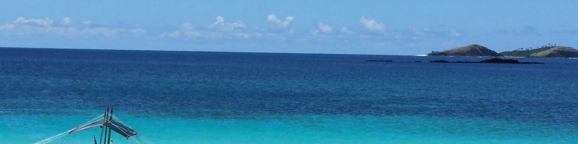 Um barco na praia, com águas turquesa cristalinas e uma ilha ao longe.