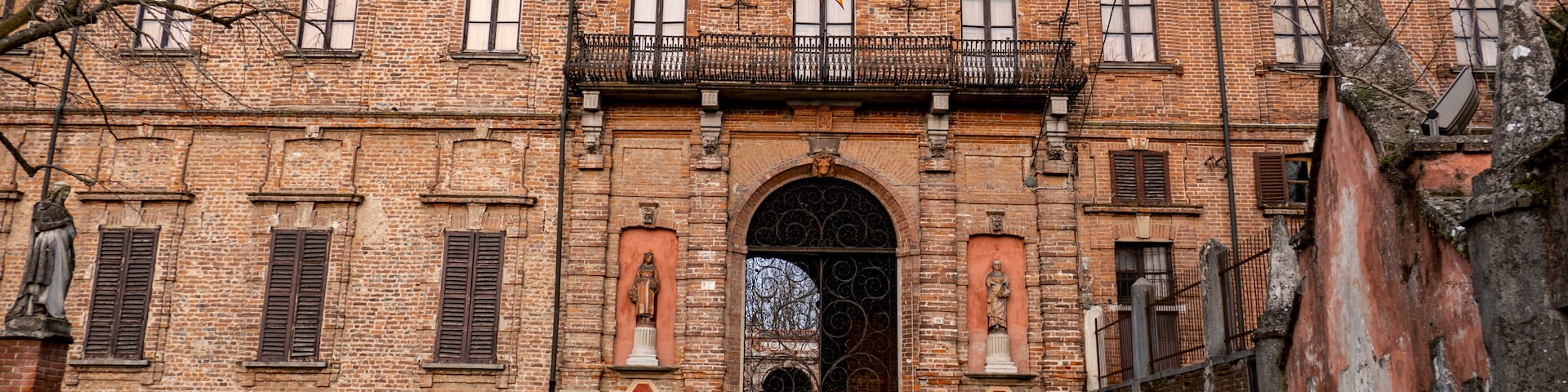 Um edifício histórico de tijolos com um arco central, estátuas e uma bandeira.