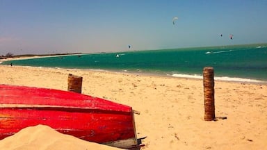 Uma praia com um barco vermelho, areal arenoso e mar azul cristalino.