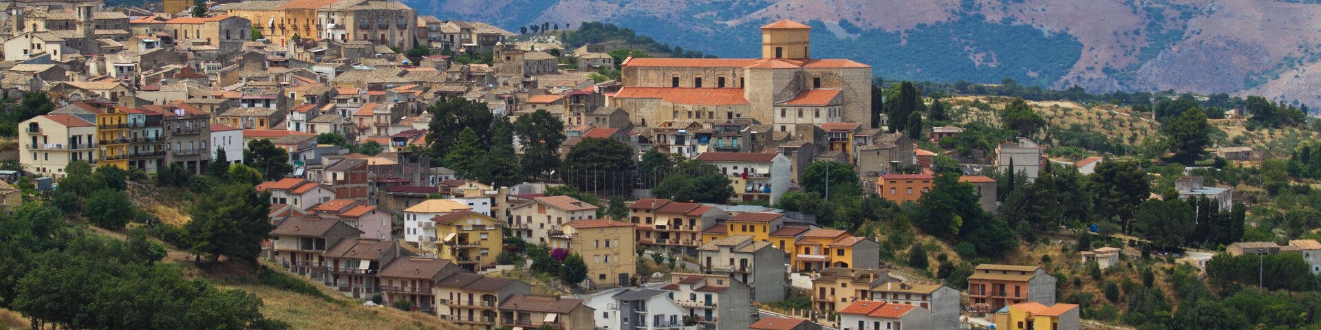 Uma vila em encosta com edifícios históricos e uma torre de igreja imponente.