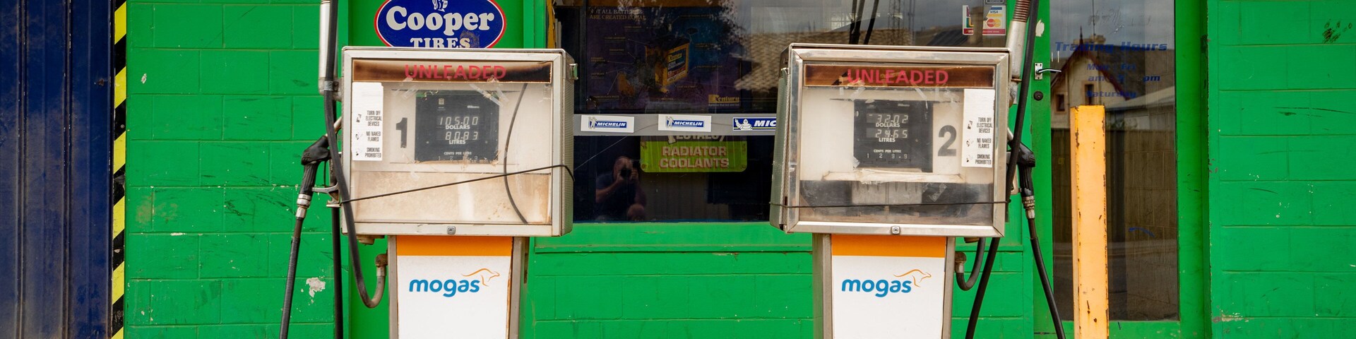 Duas bombas de combustível em um posto de gasolina com fachada verde e um anúncio da Michelin.