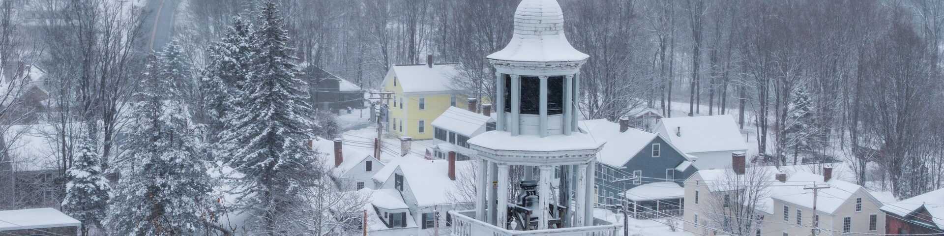 Uma cidade coberta por neve, com uma torre do relógio imponente, um campanário de igreja e um céu claro.