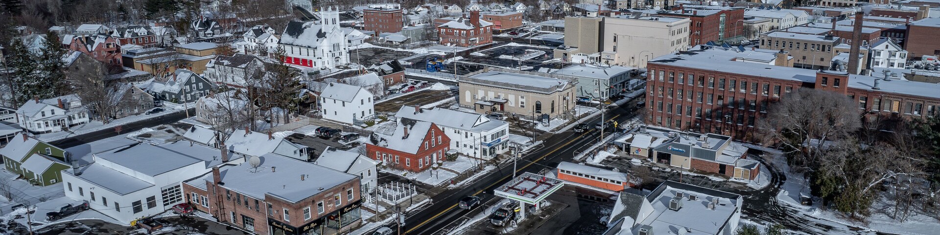 Uma cidade coberta de neve com edifícios históricos, um rio e montanhas ao fundo.