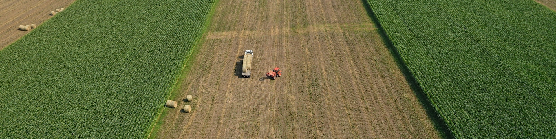 Vista aérea de um extenso campo agrícola com um trator e fardos de feno.