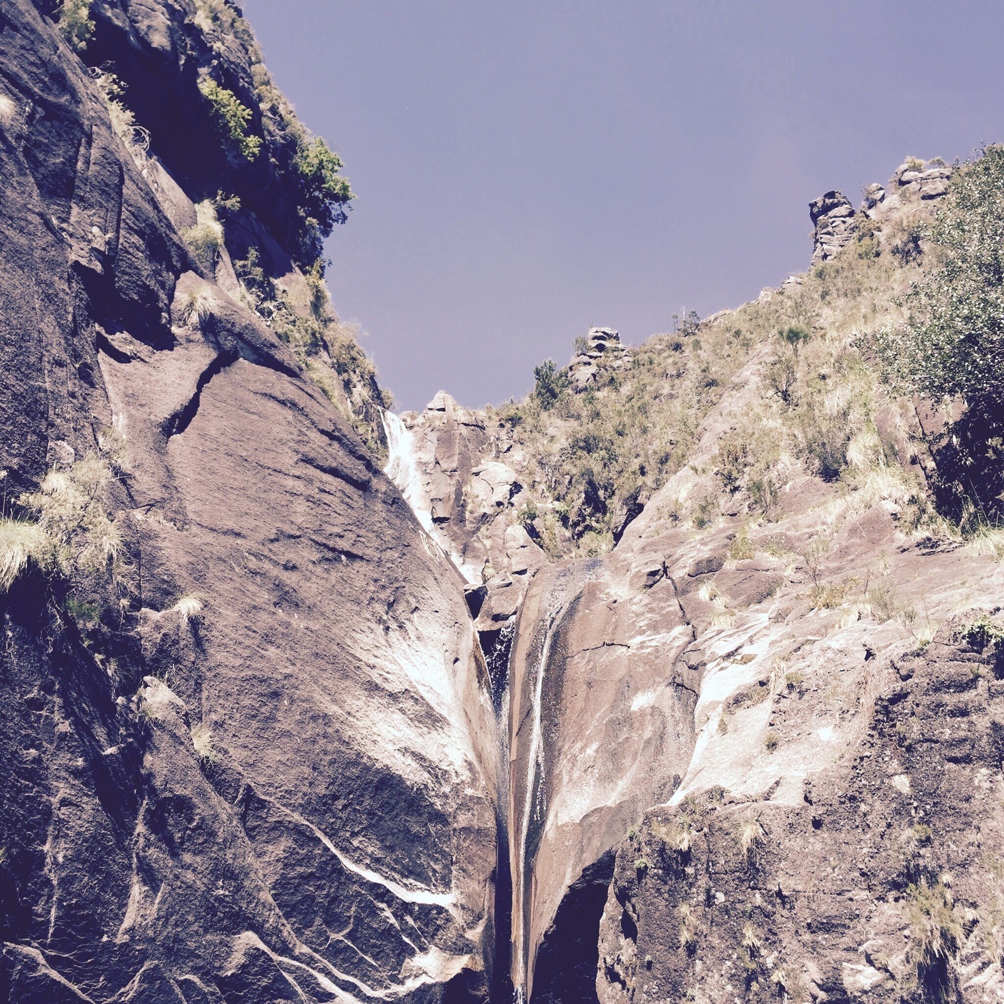 Uma cascata desce por um penhasco rochoso, rodeada por vegetação escassa.