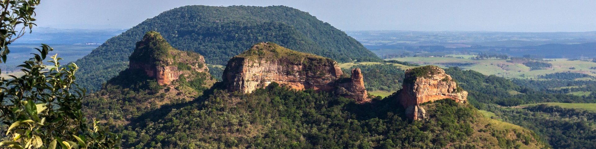Paisagem montanhosa com formações rochosas imponentes e vegetação verde densa.