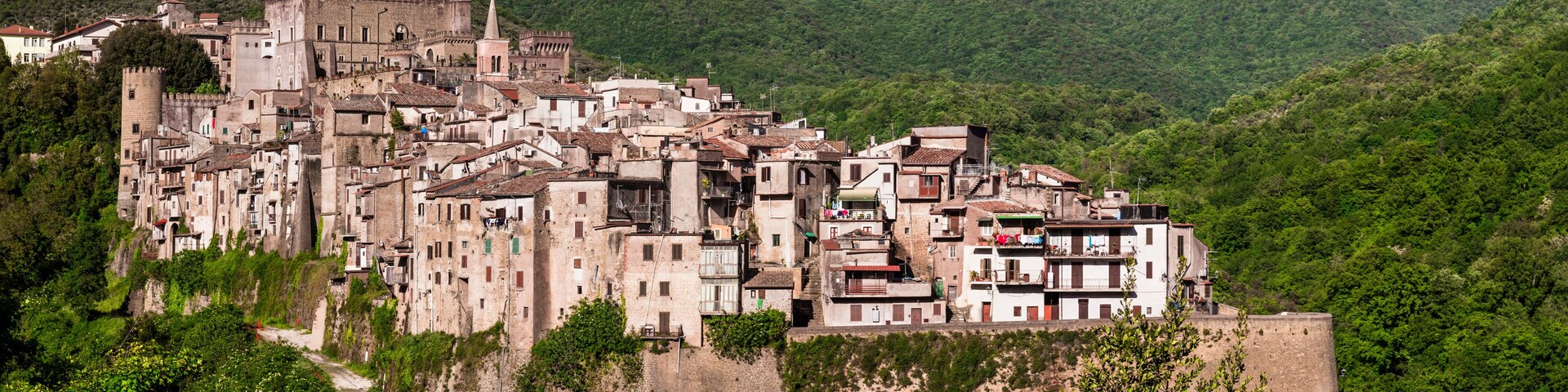 Uma cidade histórica construída numa encosta, com arquitetura medieval, rodeada por montanhas verdejantes.