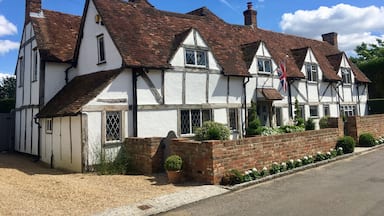 Um edifício tradicional em estilo Tudor, com paredes brancas e telhados de telhas vermelhas, cercado por um muro de tijolos e uma entrada com calçamento de brita.