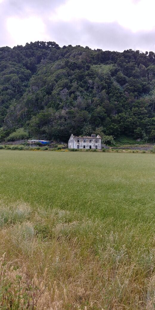 Paisagem rural com um grande campo em primeiro plano e uma casa numa colina ao fundo.