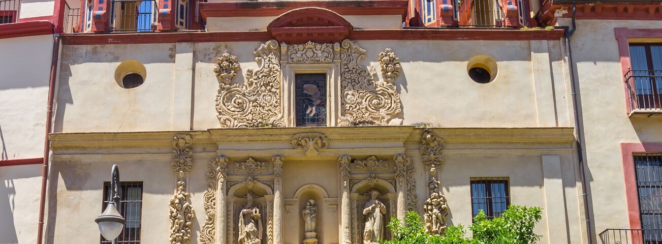 Um edifício histórico com duas torres, fachada ornamentada e uma grande porta de madeira.